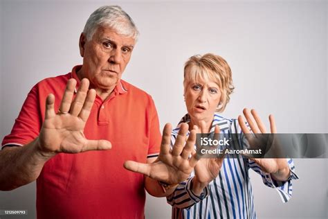 고립 된 흰색 배경 위에 함께 서있는 선임 아름다운 부부는 두려움과 역겨운 표정으로 거절과 거부를 보여주는 손바닥을 멀리 이동합니다 중지하고 금지 2명에 대한 스톡 사진 및