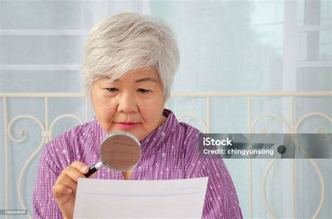 나이가 들면서 시력이 나빠지면서 렌즈를 통해 핸드헬드 문서에 읽는 돋보기를 사용하는 노인 여성 돋보기 광학 기기에 대한 스톡