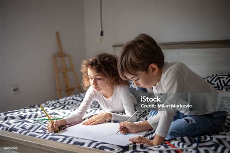 두 자녀 형제 자매는 침실의 침대에서 나무 크레용으로 종이에 그림을 그립니다 10 11세에 대한 스톡 사진 및 기타 이미지