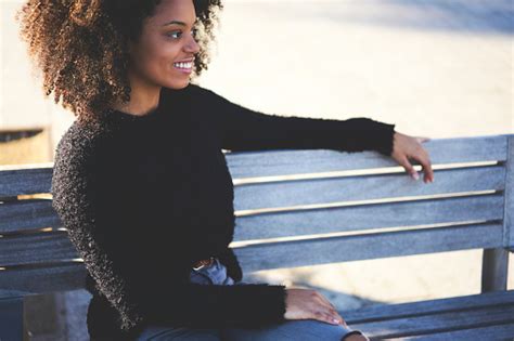 매력적인 아프리카 미국 여성 보고 멀리 야외 나무 벤치에 앉아 여가 시간을 즐기는 동안 웃 고 선샤인 거리에 레크 데 좋은 분위기에서 아름 다운 젊은 Hipster 소녀