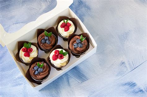 크림 치즈와 초콜릿 컵케이크와 신선한 블루베리 라즈베리를 화이트 페이퍼 박스 블루 배경에 곁들인 컵케이크 배달 상자에 베리 컵 케이크 달콤한 음식 배달 거품 내기에 대한