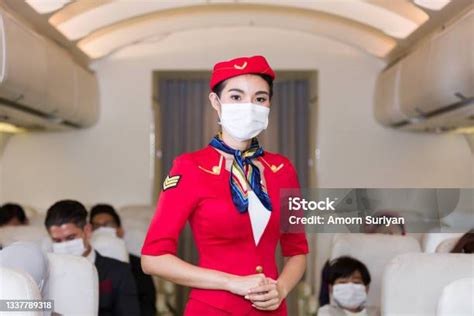 매력적인 승무원 비행기의 보호 얼굴 마스크 모자 빨간 드레스 정장을 입은 에어 호스티스 또는 스튜어디스의 초상화 비행기에서 보호 얼굴 마스크를 착용한 여행자 또는 승객