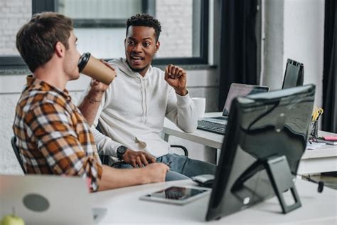 Premium Photo Two Young Multicultural Programmers Talking While Sitting Together In Office