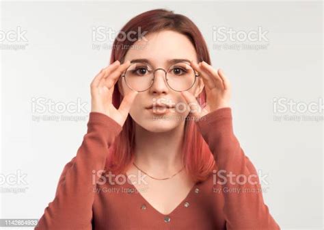 여러 가지 빛깔의 머리카락이 있는 아름 다운 소녀는 안경의 테두리 뒤에 두 손을 쥐고 그녀 앞에 있는 것을 봅니다 스튜디오에서 흰색 배경에 고립 교육에 대한 스톡 사진 및