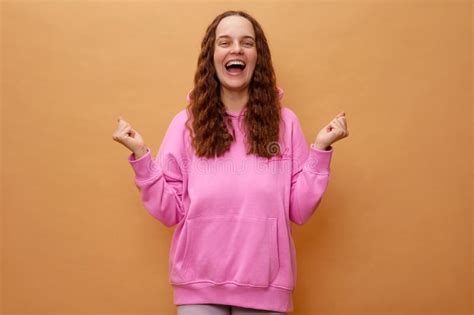 A Cheerful Young Woman With Long Wavy Hair Smiles Widely While Raising