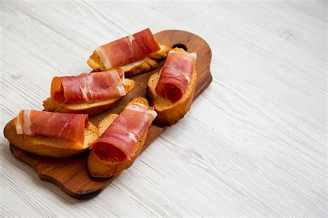 흰색 나무 배경 측면 보기에 나무 보드에 세라 노 햄과 Crostini 공간에 복사 합니다 도마 요리 도구에 대한 스톡 사진 및