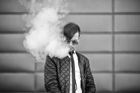 Vape 남자입니다 비행 선글라스 Vaping에 전자 담배에서 증기 시키는 현대이 발과 잘생긴 젊은 백인 남자의 초상화 흑인과