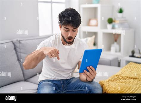 Hispanic Man With Beard Using Touchpad Sitting On The Sofa Pointing
