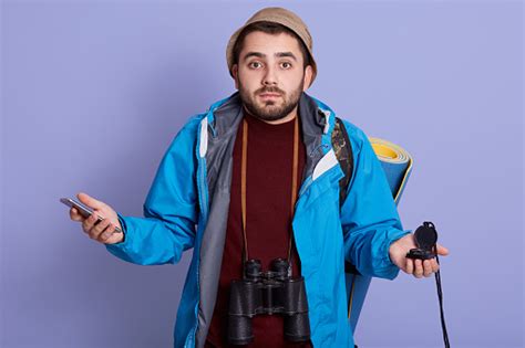 잃어버린 여행자는 라일락 배경위에 고립 된 포즈를 취하고 파란색 재킷 셔츠 및 모자를 쓰고 무기력한 표정을 가진 남자 숲에서