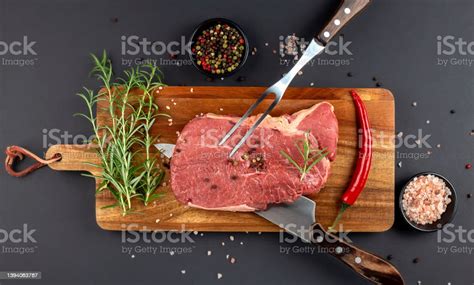 나무 커팅 보드에 고기와 신선한 로즈마리와 향신료를위한 칼과 포크로 요리하는 생 쇠고기 스테이크 검은 색 배경 0명에 대한 스톡