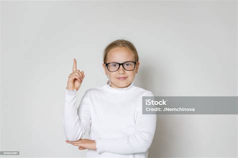 안경을 쓴 귀여운 진지한 소녀가 하얀 스튜디오 벽 배경에 있는 복사 공간을 가리키고 있다 8 9 살에 대한 스톡 사진 및 기타