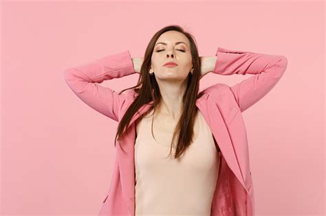 스튜디오에서 파스텔 분홍색 벽 배경에 고립 된 머리 뒤에 손을 잡고 눈을 유지 재킷을 입고 편안한 여자의 초상화 사람들은