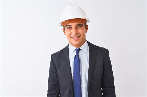 섹시한 표정 명랑하고 행복한 얼굴로 카메라를 보고 고립 된 흰색 배경 윙크 위에 양복과 헬멧을 착용한 젊은 잘생긴 건축가 남자 건설 산업에 대한 스톡 사진 및 기타 이미지