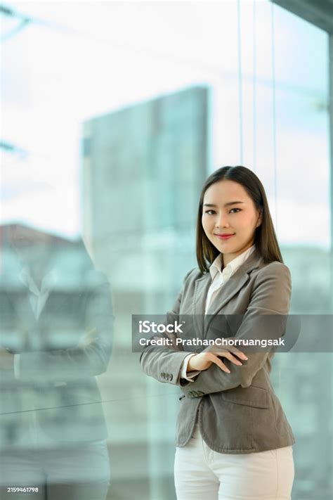 우아한 양복을 입은 자신감 있는 아시아 사업가의 초상화가 현대 사무실의 창문 근처에 팔짱을 끼고 서 있습니다 25 29세에 대한