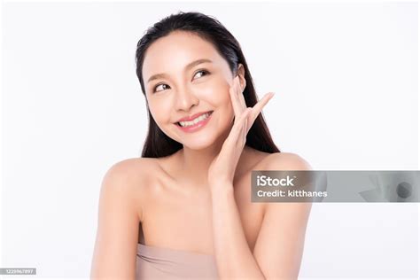 흰색 배경 뷰티 화장품 및 얼굴 치료 개념에 고립 된 신선한 건강한 피부로 깨끗한 얼굴을 만지는 아름다운 젊은 아시아 여성