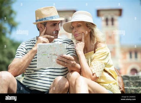 Portrait Of Senior Couple Reading Map While Sitting On Bench Stock