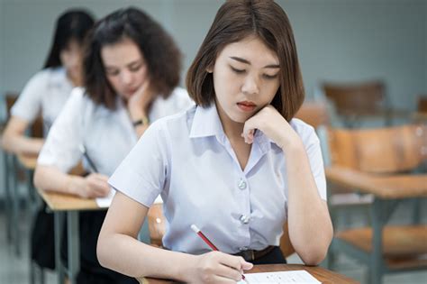 강의 의자에 앉아 교실에서 시험 용지 답변 시트에 쓰는 십대 대학생의 선택적 초점은 교실에서 유니폼을 입은 대학생 강사에 대한