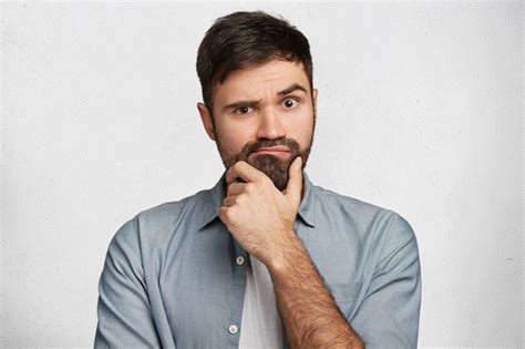 Portrait Of Displeased Male Frown Face Keeps Hand On Chin Wears Denim