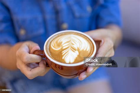 뜨거운 커피 머그잔 커피에 라떼 아트 잎 모양의 우유 거품 여자의 손에 아름다운 뜨거운 라떼 아트 전문 바리스타 아티스트의 나무 테이블에 놓인 커피 아트의 평면도 45 49
