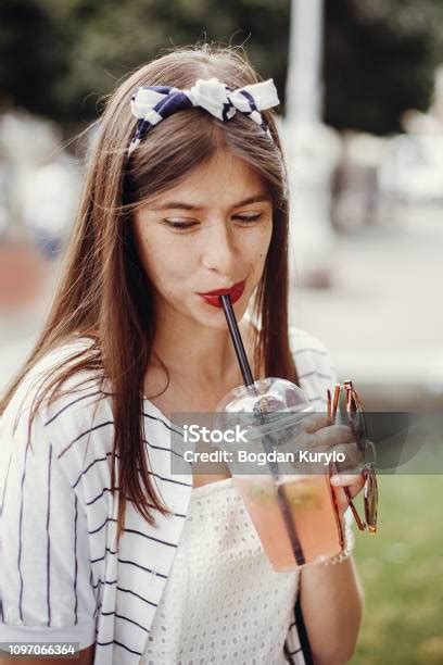 행복 한 Hipster 레모네이드를 마시는 밀 짚 플라스틱 컵을 들고과 복고풍 드레스와 머리 띠 소녀 아름 다운 세련 된 젊은 여자 음료를 들고와 도시의 거리에서 머리밴드에