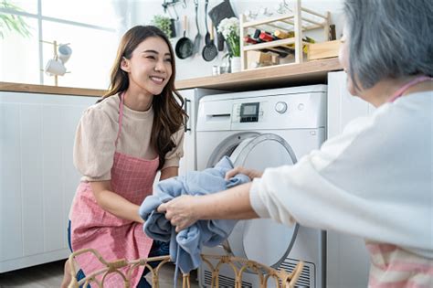 집에서 부엌에서 집안일과 집안일을하는 아시아 사랑스러운 가족 어린 소녀 딸이 노인 어머니를 돕고 지원하기 위해 세탁기에 옷을