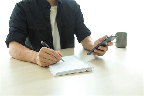 젊은 남자가 카페 레스토랑에서 책상에 커피 컵을 들고 디지털 모바일 스마트 폰을 쓰고 작업합니다 45 49세에 대한 스톡 사진