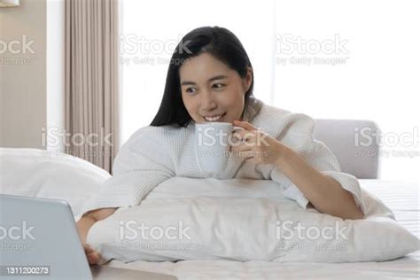 침대에 노트북에서 작업 목욕 가운에 행복 아름다운 아시아 여성 여자는 침실에서 커피 한 잔과 함께 침대에 누워 침대에 어린