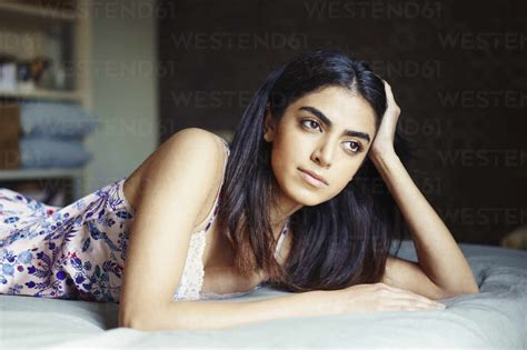 Portrait Of Pensive Young Woman Lying On Bed Looking At Distance Stock