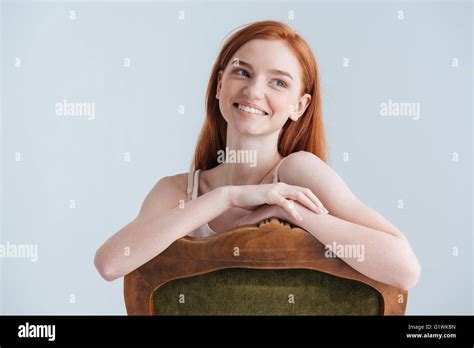 Smiling Redhead Woman Sitting On The Chair And Looking Away Isolated On A White Background Stock