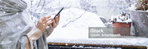 따뜻한 모자와 담요를 두른 여성이 스마트폰을 손에 들고 있다 눈이 내리는 겨울 풍경 겨울에 대한 스톡 사진 및 기타 이미지 겨울 휴대전화 눈보라 Istock