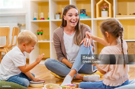 유치원 교사는 바닥에 앉아서 다양한 악기와 타악기를 사용하여 음악 수업을 듣는 아이들 교사 교육 관련 직업에 대한 스톡 사진 및 기타 이미지 교사 교육 관련 직업 어린