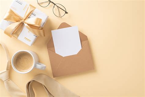 넥타이 안경 리본 리본이 달린 선물 상자 엽서가 있는 공예 종이 봉투 텍스트나 광고를 위한 빈 공간이 있는 베이지색 배경에 커피 머그잔을 볼 수 있어 아버지의 날을 기억에