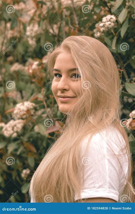 Young Natural Blonde Woman Standing In Front Of A Flowering Bush Stock
