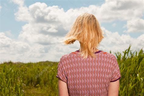 Back Of Woman With Blond Hair In Field Of High Grass Blue Cloudy Sky