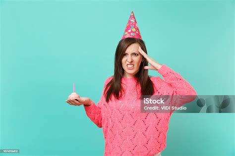 염증된 젊은 여자 니트 핑크 스웨터 생일 모자를 머리에 씌우고 손에 손에 촛불 파란색 배경 스튜디오 초상화에 고립 된 케이크 개최 사람들의 라이프 스타일 개념입니다 복사