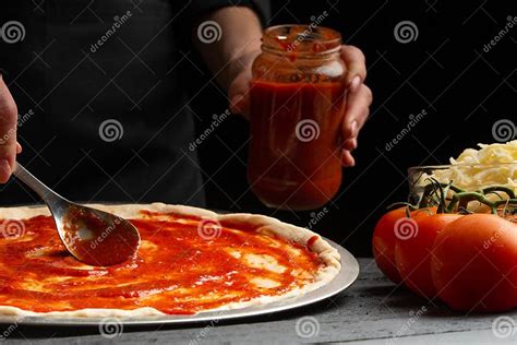 Chef Smears Italian Pizza With Sauce On Black Background Close Up