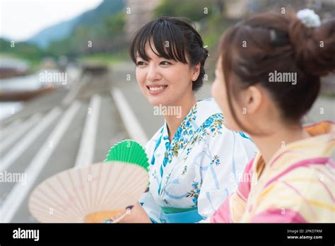 Two Women In Yukata Holding And Smiling With A Fan On The Riverbank