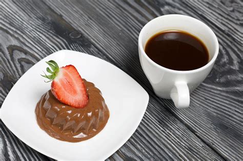 꽃잎이 달린 딸기 반으로 장식된 초콜릿 퍼지 커피 한 잔 디저트접시는 검은색과 흰색으로 칠해진 양모 소나무 보드에 서 있습니다