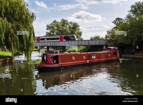 A Red Canal Boat Turns On The River Great Ouse As A Train Appoaches Ely