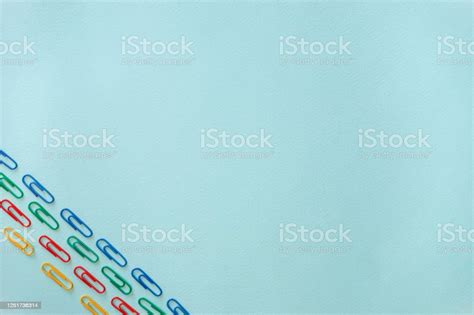 밝은 파란색 배경에 파란색 녹색 빨간색 및 노란색 종이 클립의 수평 미니멀 클로즈업 플랫 레이 구성 왼쪽 아래 모서리에 있는