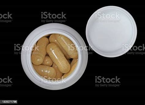 검은 색 배경에 모자와 흰색 병 이나 플라스틱 캐니스터에 노란색 캡슐 또는 알 약의 상단 보기를 닫습니다 병 뚜껑에 대한 스톡