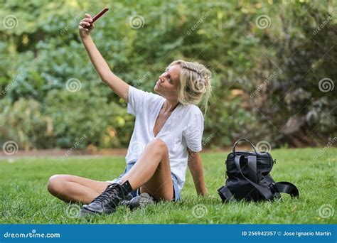 Young Woman Taking Selfies With A Mobile Phone While Sitting On Grass Outdoors Stock Image