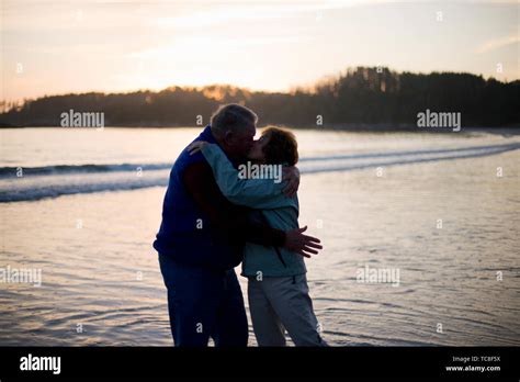 Mature Couple Kissing At The Waters Edge At Sunset On A Beach Stock
