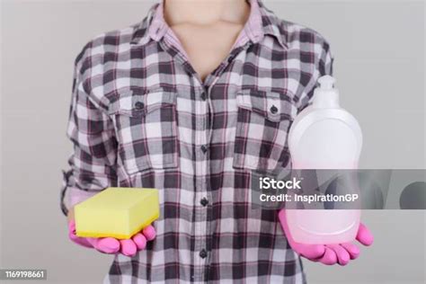 접시 투명 식기 세척 폼 더러운 캐주얼 체크 셔츠 핑크 천 사람 가족 개념 회색 배경에 고립 된 노란색 스폰지 병을 보여주는 예쁜 아가씨의 사진을 클로즈업 가사 집안일에