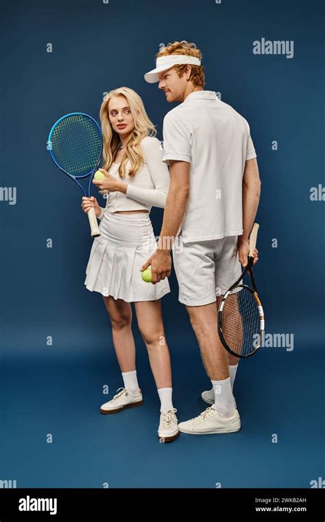 Full Length Of Young Couple In White Tennis Attire With Racquets And