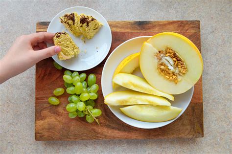 수제 케이크 조각 멜론 조각 접시 나무 배경에 녹색 포도 신선한 과일과 건강 식품의 개념이있는 여성의 손 개체 그룹에 대한 스톡