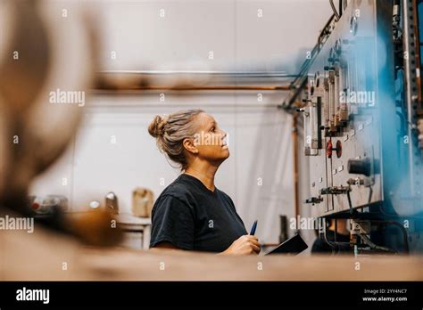 Side View Of Mature Female Worker Examining Circuit In Metal Factory
