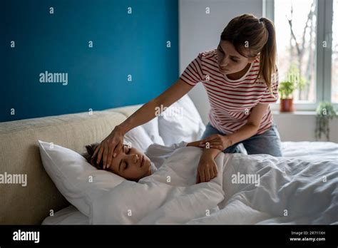 Sick Teenage Girl Lying In Bed Having Chills And Fever Mom Checking Temperature Touching