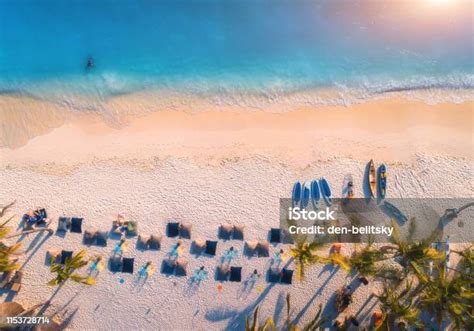 석양에 푸른 바다의 모래 해변에서 우산 손바닥의 조감도 잔지바르 아프리카에서 여름 여행 야자수 파라솔 사람 모래 파도와 열 대 풍경입니다 공중에서 탑 뷰 경관에 대한 스톡