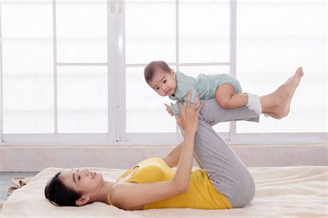 아름다운 아시아 엄마와 딸이 집에서 요가 운동을 하고 있다 젊은 엄마는 침대에서 비행기를 타고 노는 아기를 들어 올린다 행복한 엄마가 아기를 공중에 띄운다 여자와 유아는